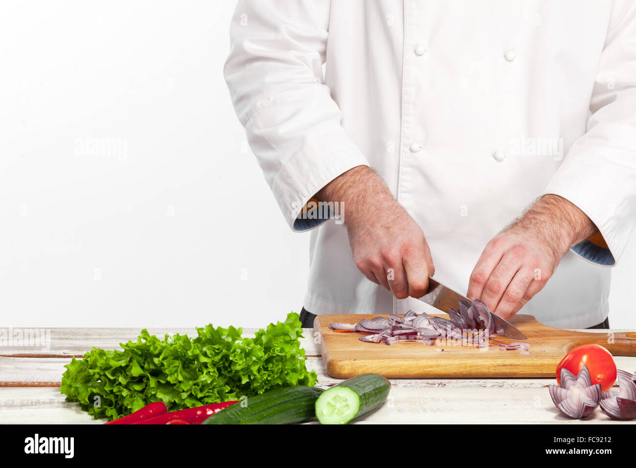 The hands of chef cutting a onion in his kitchen on white background ...