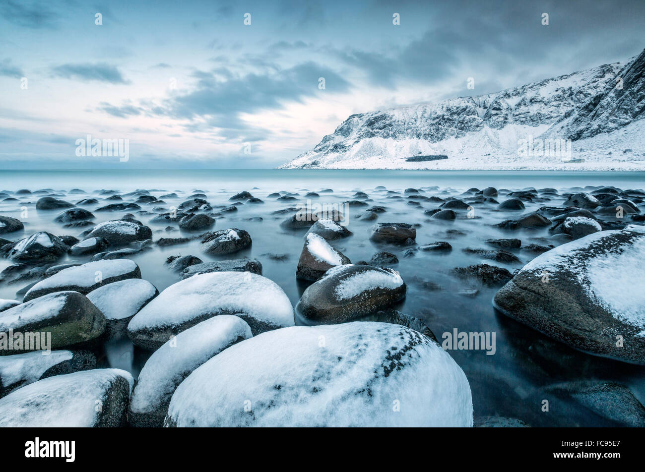 Rocks in the cold sea and snow capped mountains under the blue light of ...