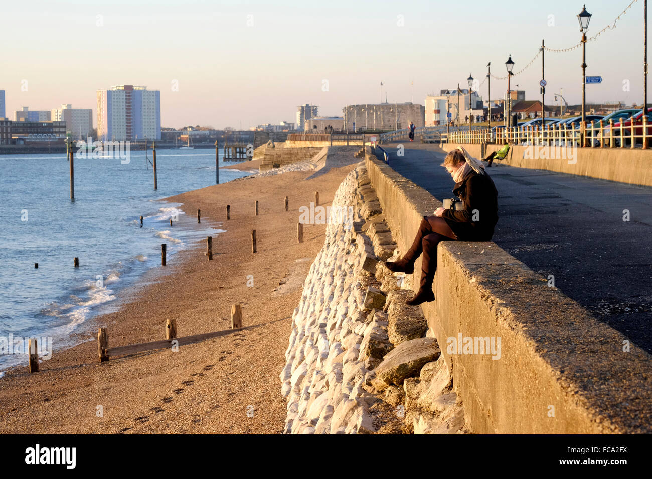 young woman sat in the golden light of sunset on southsea seafront ...
