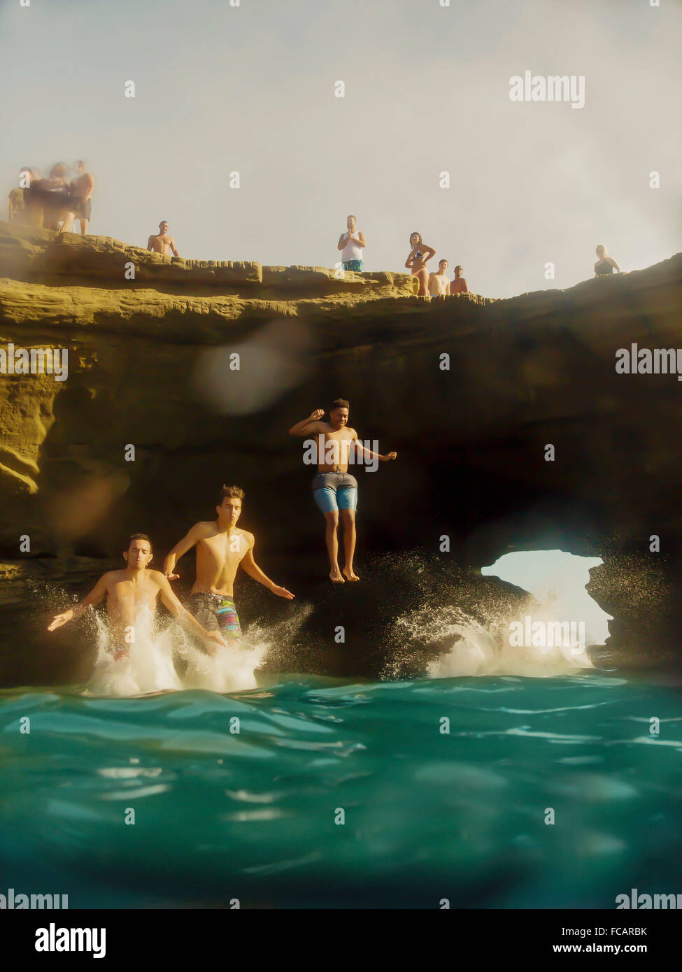 Three men dive from cliff at San Diego, California during sunset and ...