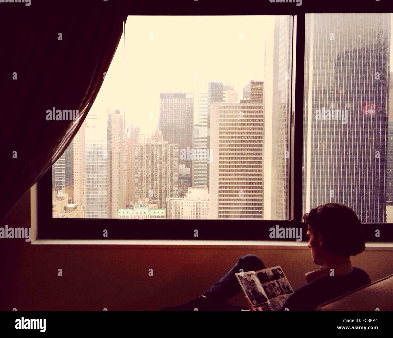 Rear View Of Man Reading Magazine By Window At Home Stock Photo - Alamy