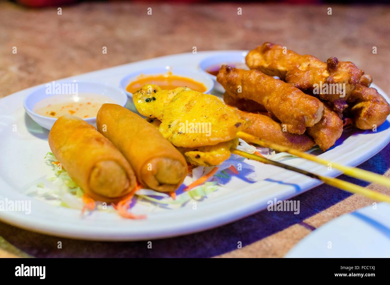 A thai food dish with fried spring rolls, satay chicken on skewers, and ...