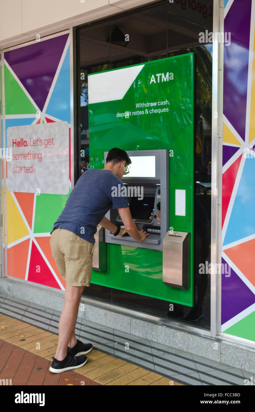 Young man at an ATM set in multi coloured wall Stock Photo - Alamy