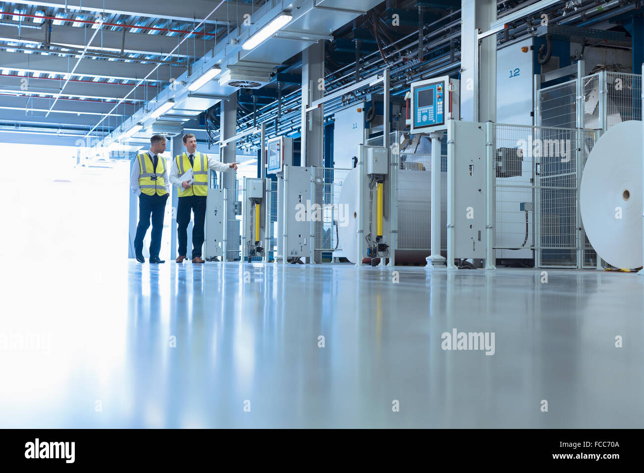 Workers walking along machinery in factory Stock Photo - Alamy