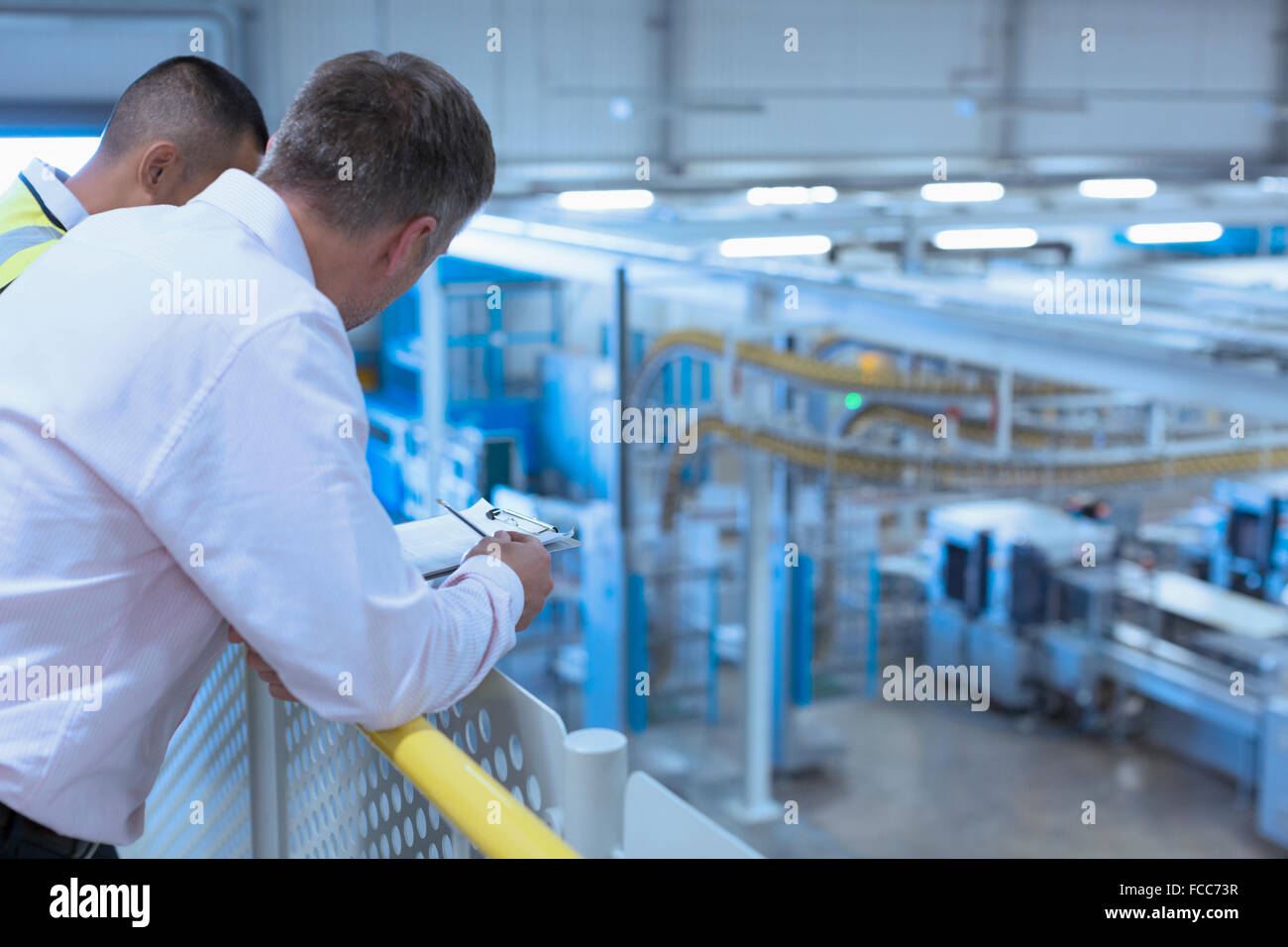 Workers leaning on railing overlooking factory Stock Photo - Alamy
