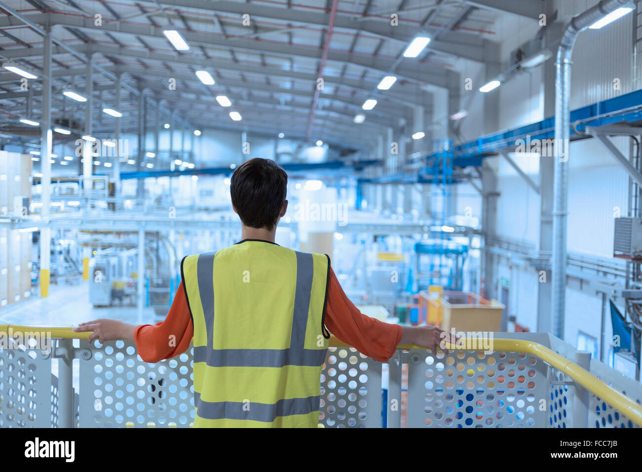 Worker in reflective clothing on platform looking out over factory ...