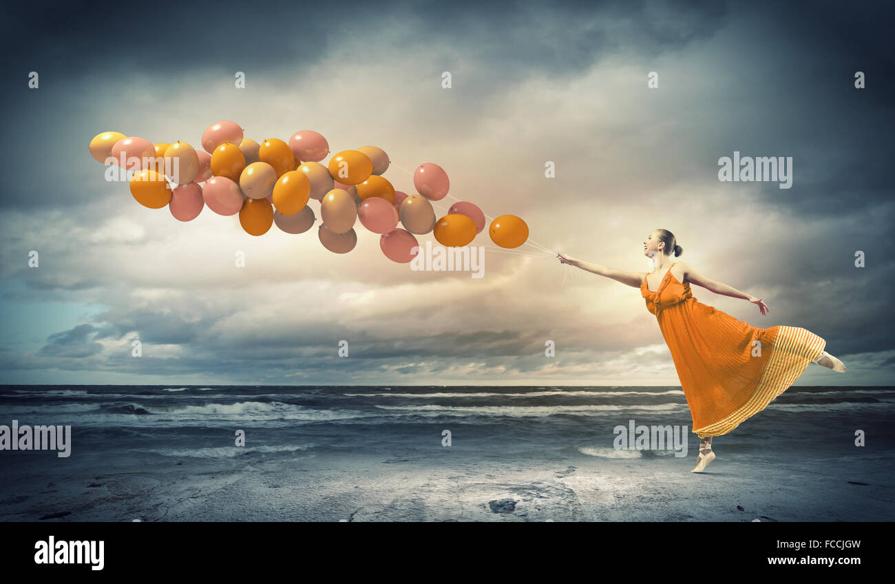 Young woman in dress and ballerinas dancing with colorful balloons ...