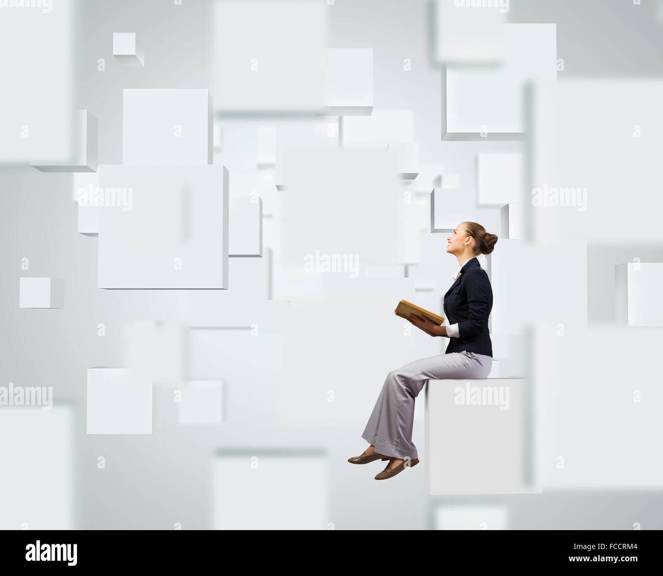 Young attractive woman sitting on white cube and reading book Stock ...