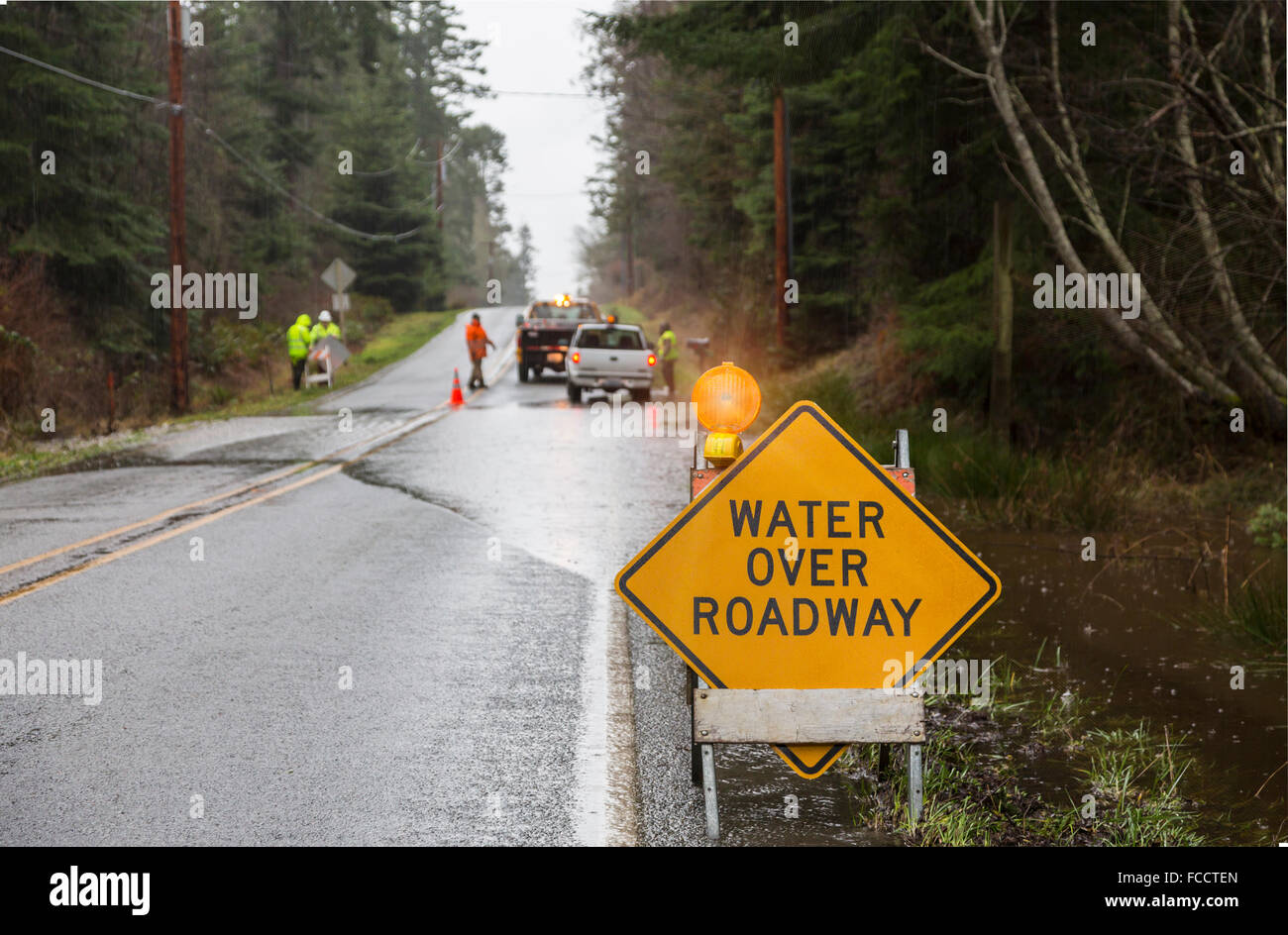 Emergency workers placing warning signs on flooded roadway in Stock ...