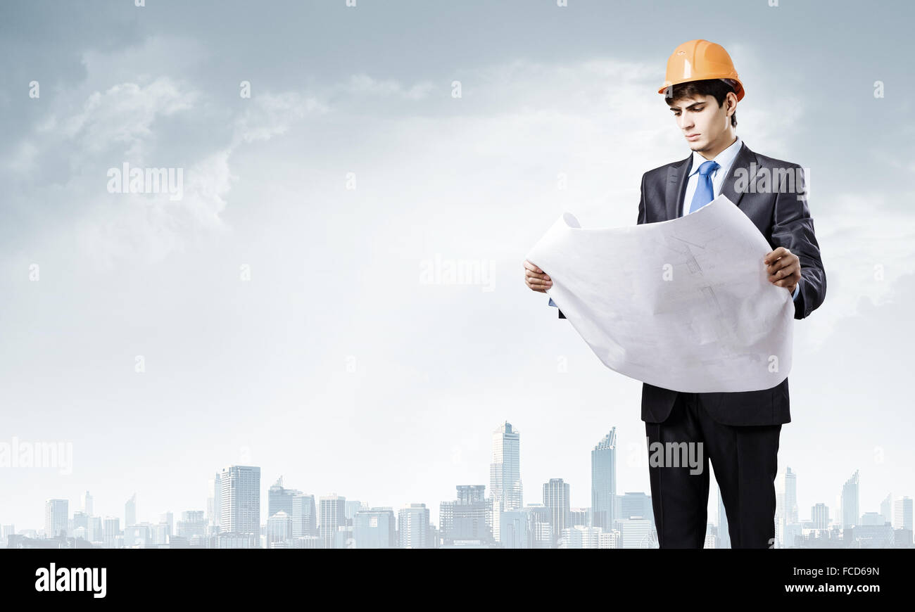 Young man engineer in helmet examining construction project Stock Photo - Alamy