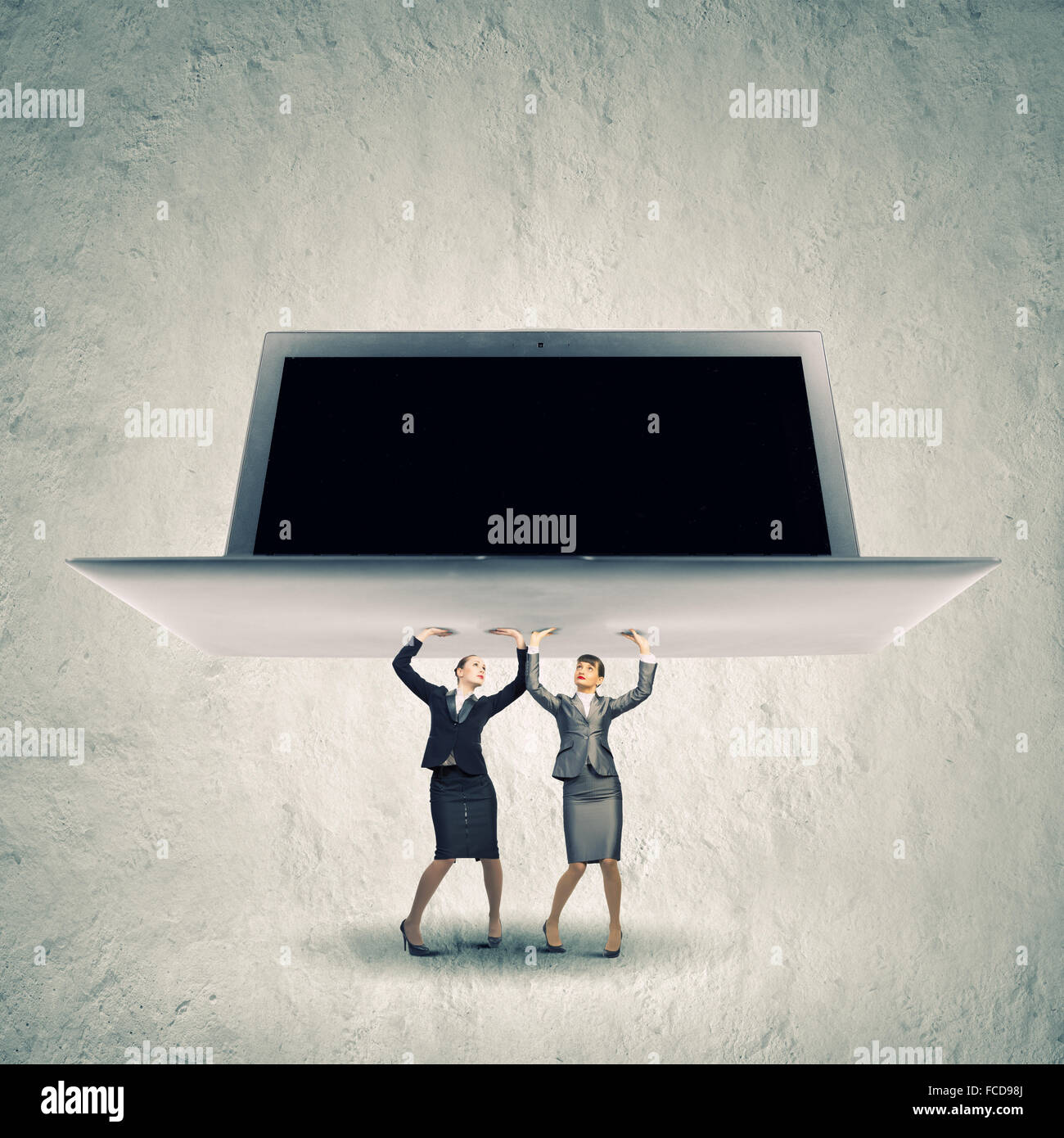 Two young businesswoman lifting huge laptop above head Stock Photo - Alamy