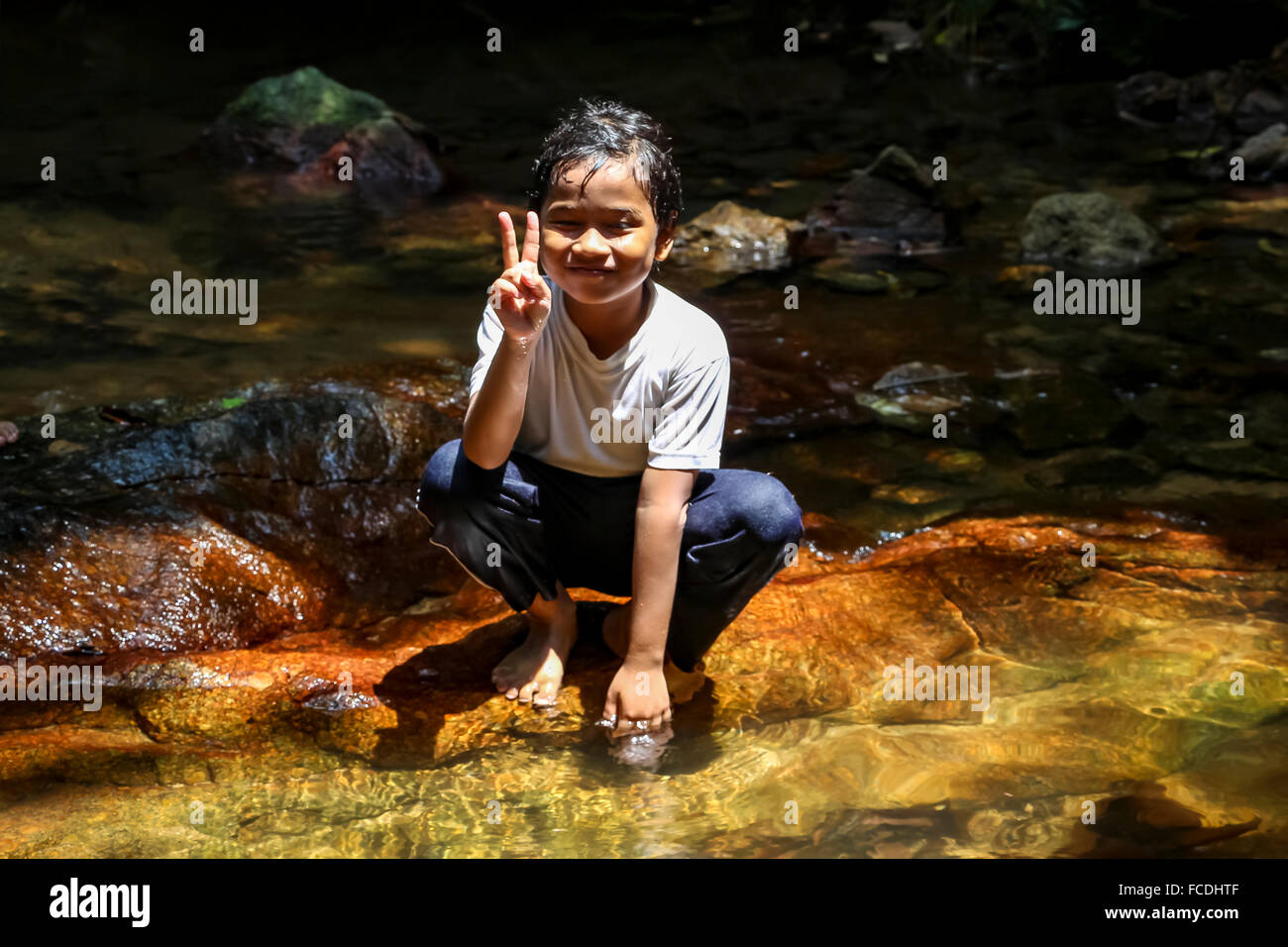 Child holding a peace sign while squatting over water Stock Photo - Alamy