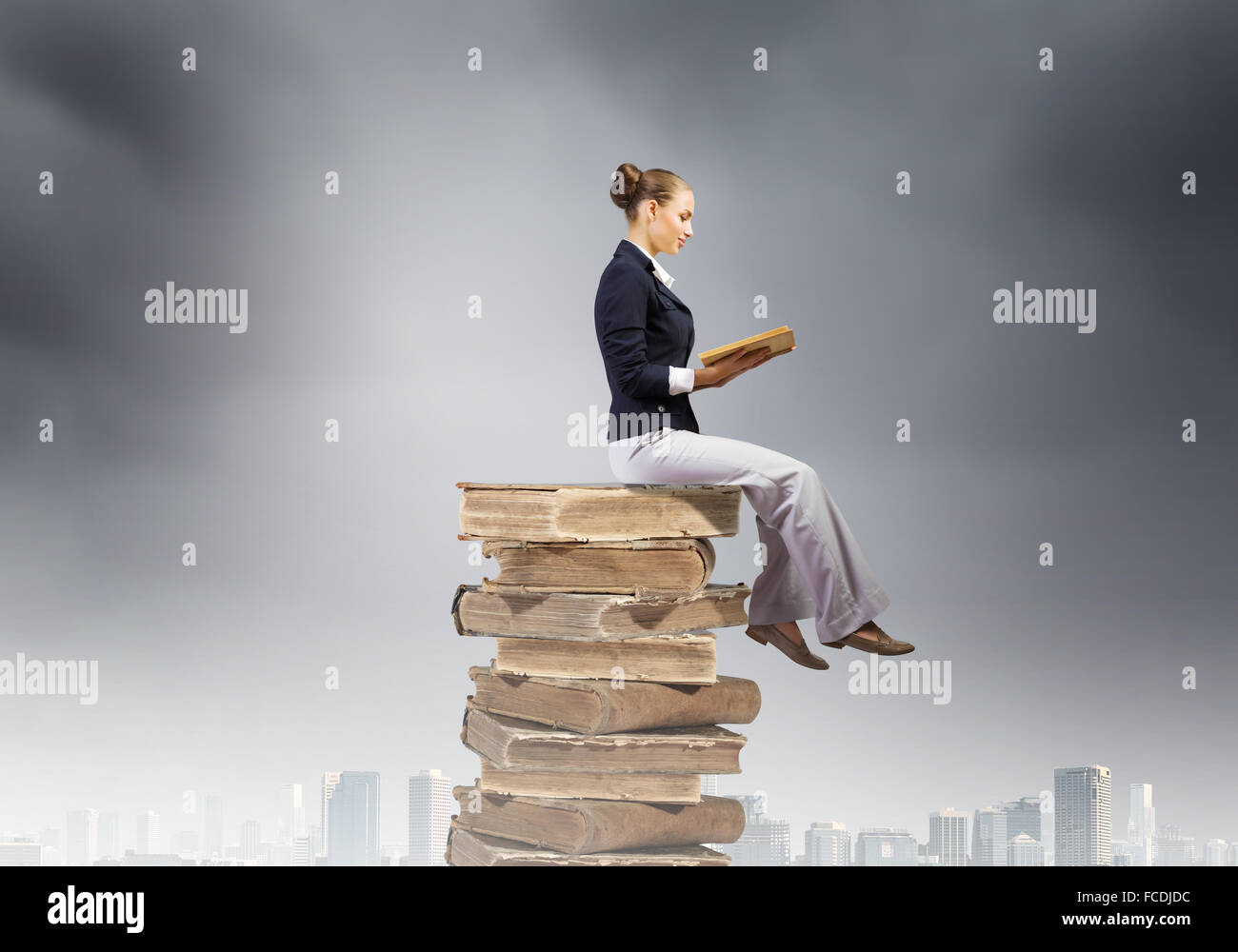 Young attractive businesswoman sitting on pile of old books reading ...