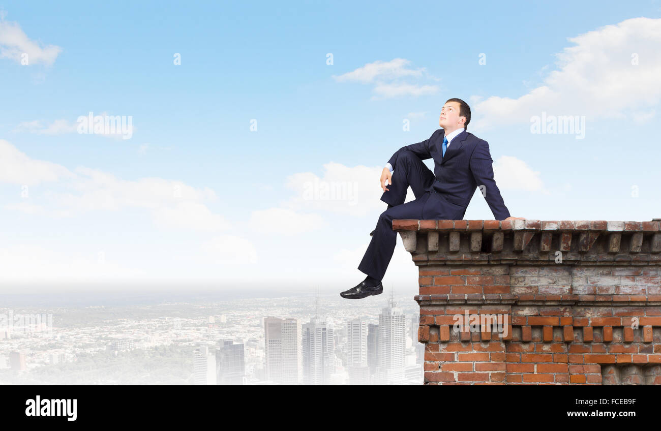 Young businessman sitting on roof of building Stock Photo - Alamy