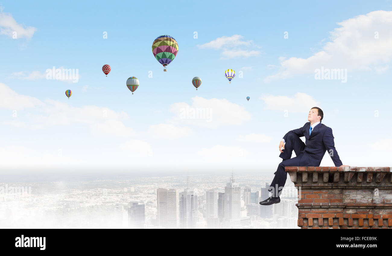 Young businessman sitting on roof of building Stock Photo - Alamy