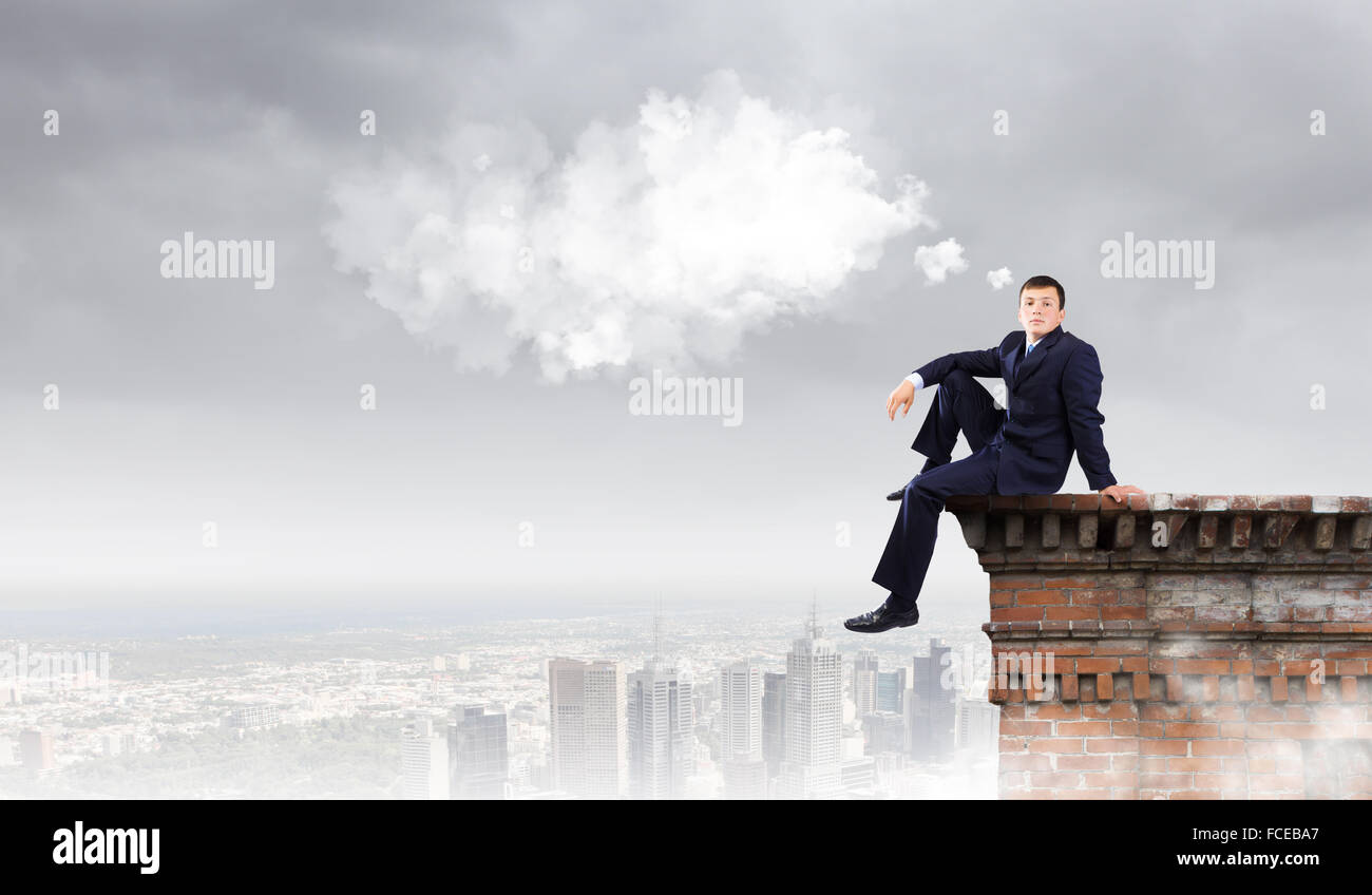 Young businessman sitting on roof of building Stock Photo - Alamy