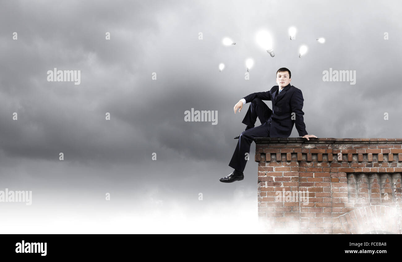 Young businessman sitting on roof of building Stock Photo - Alamy