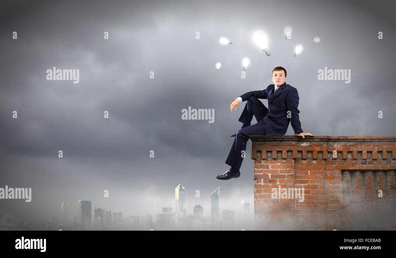 Young businessman sitting on roof of building Stock Photo - Alamy