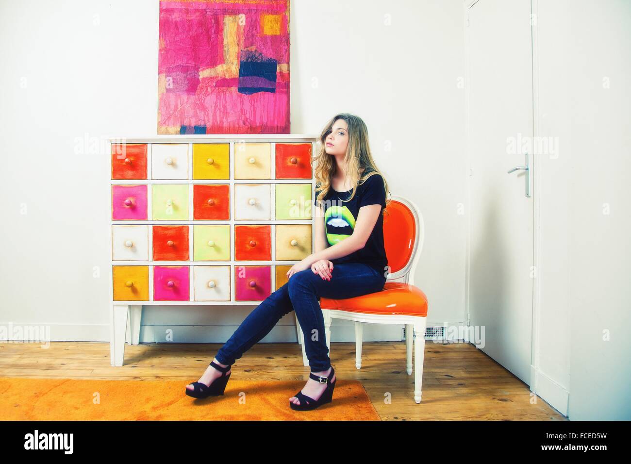 Woman sitting on a red chair in a colorful room Stock Photo - Alamy