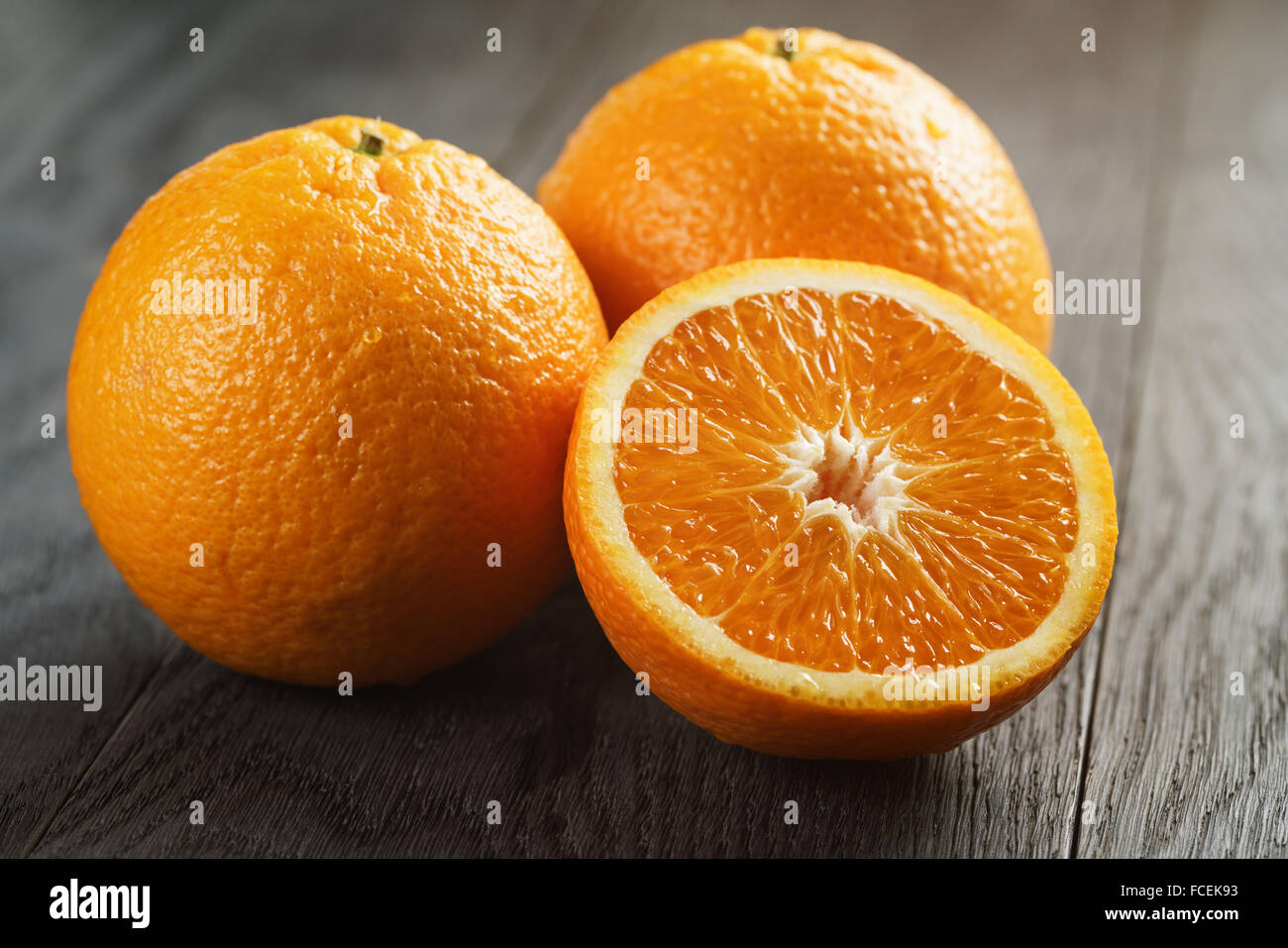 three ripe oranges on wooden table one half cut Stock Photo - Alamy