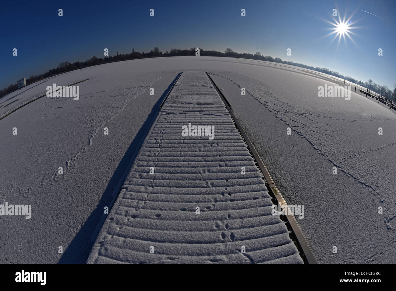 The sun shines above snow-covered jetty stretching out into lake ...