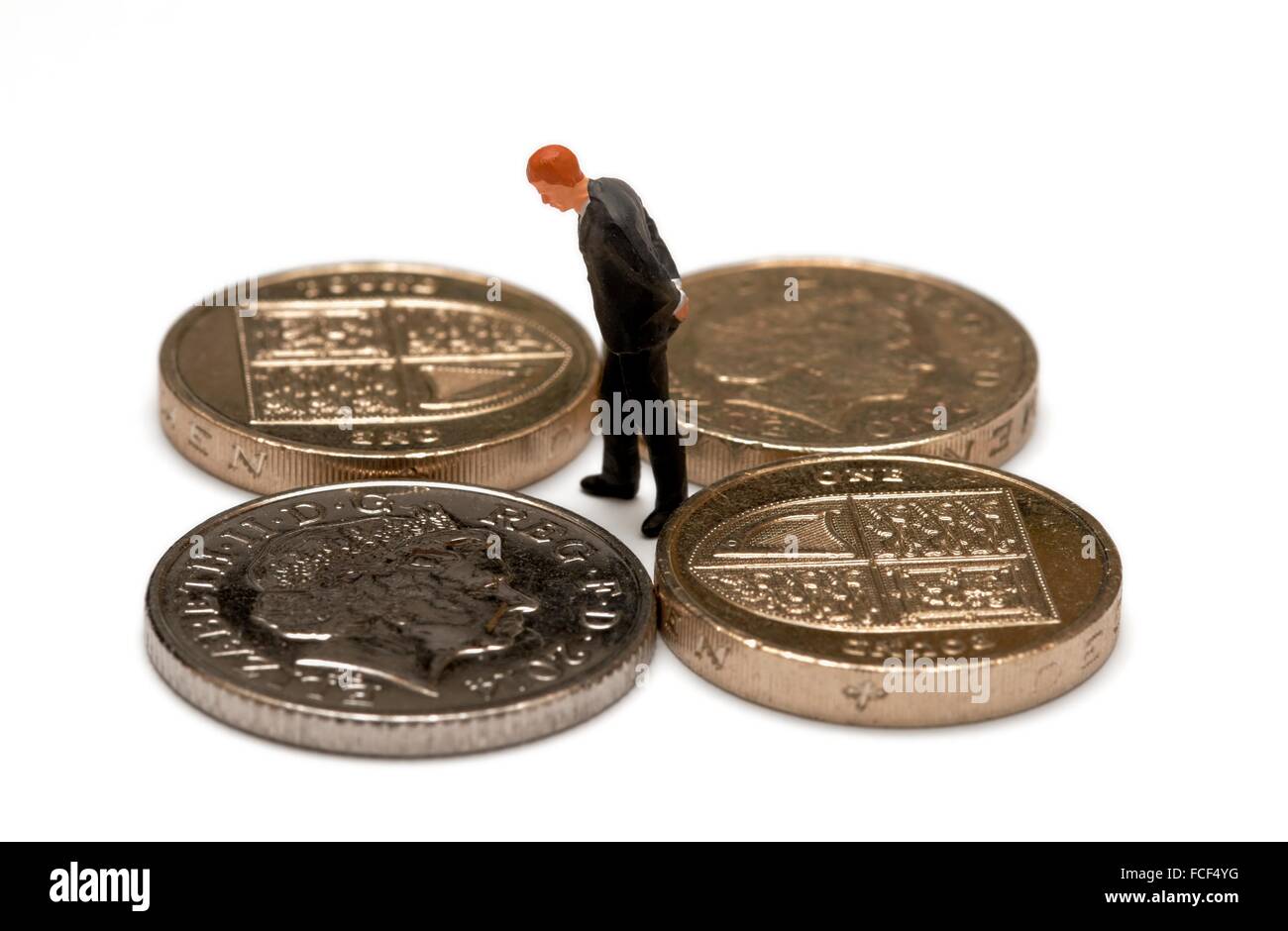 A Miniature figurine man in a suit looking at one pound coins and a ten ...