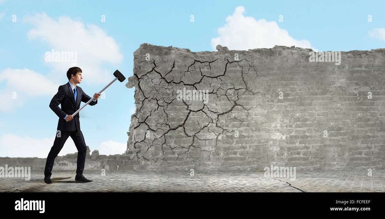 Young determined businessman breaking wall with hammer Stock Photo - Alamy