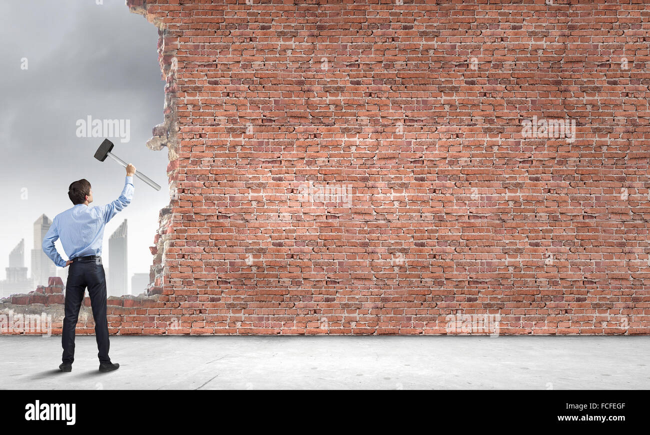 Young determined businessman breaking wall with hammer Stock Photo - Alamy