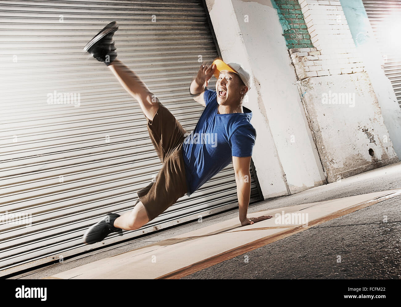 A young man breakdancing on the street of a city, balancing on one hand ...