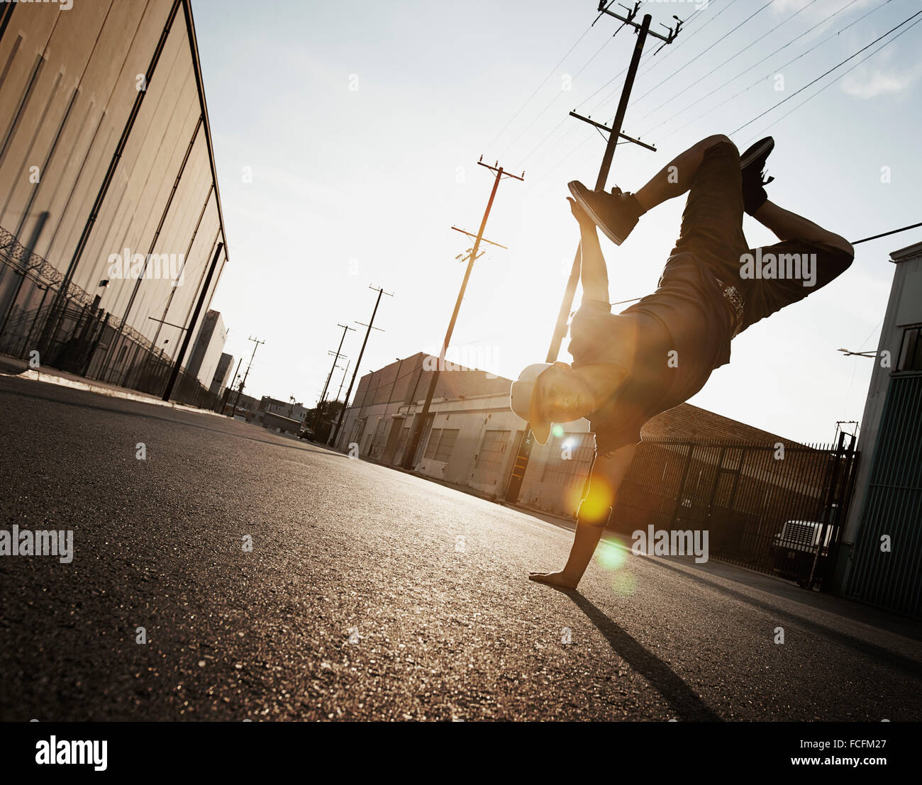 A young man breakdancing on the street of a city, doing a one handed ...