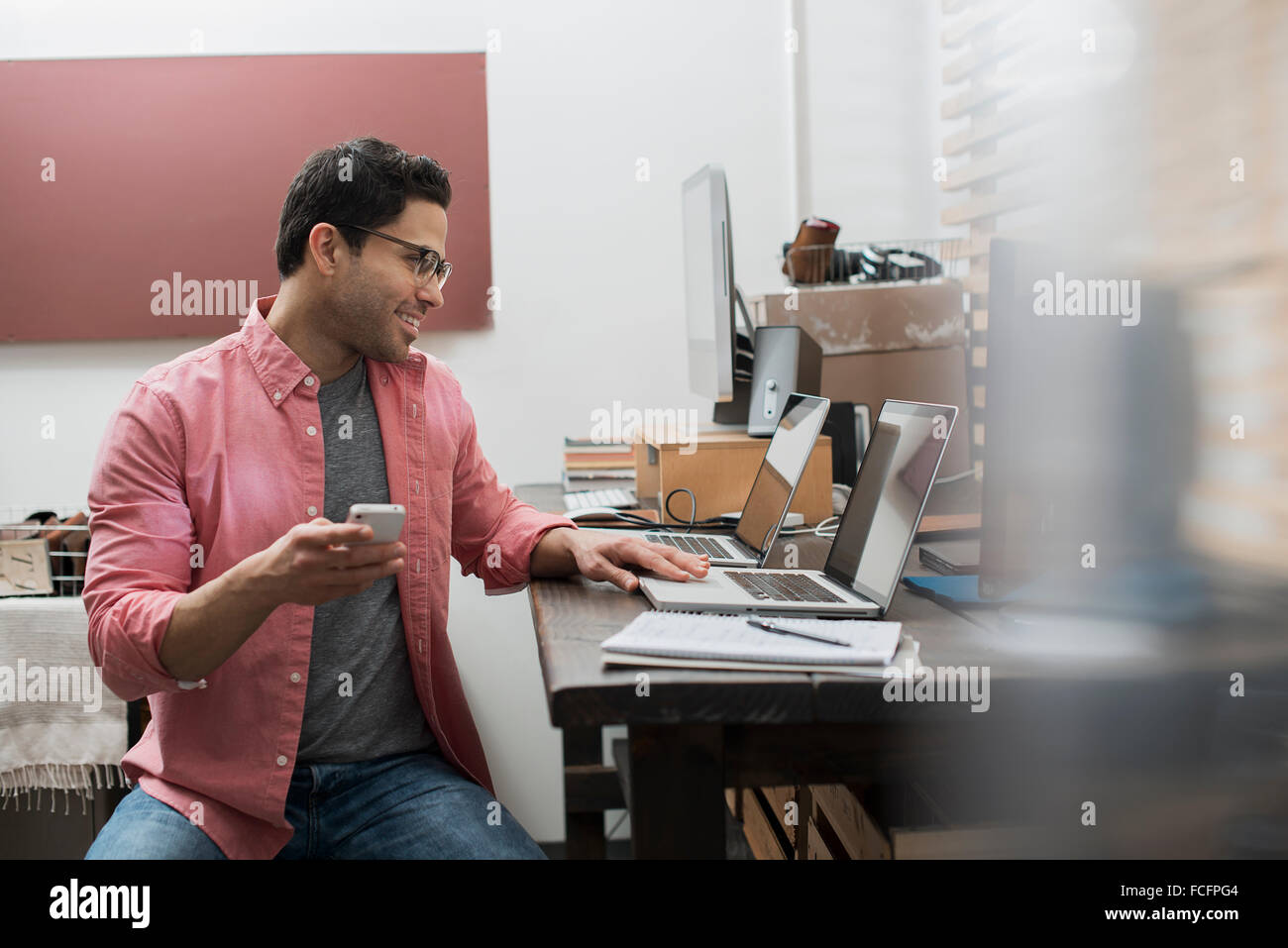 A man in a home office with a desk with two laptops, checking ...