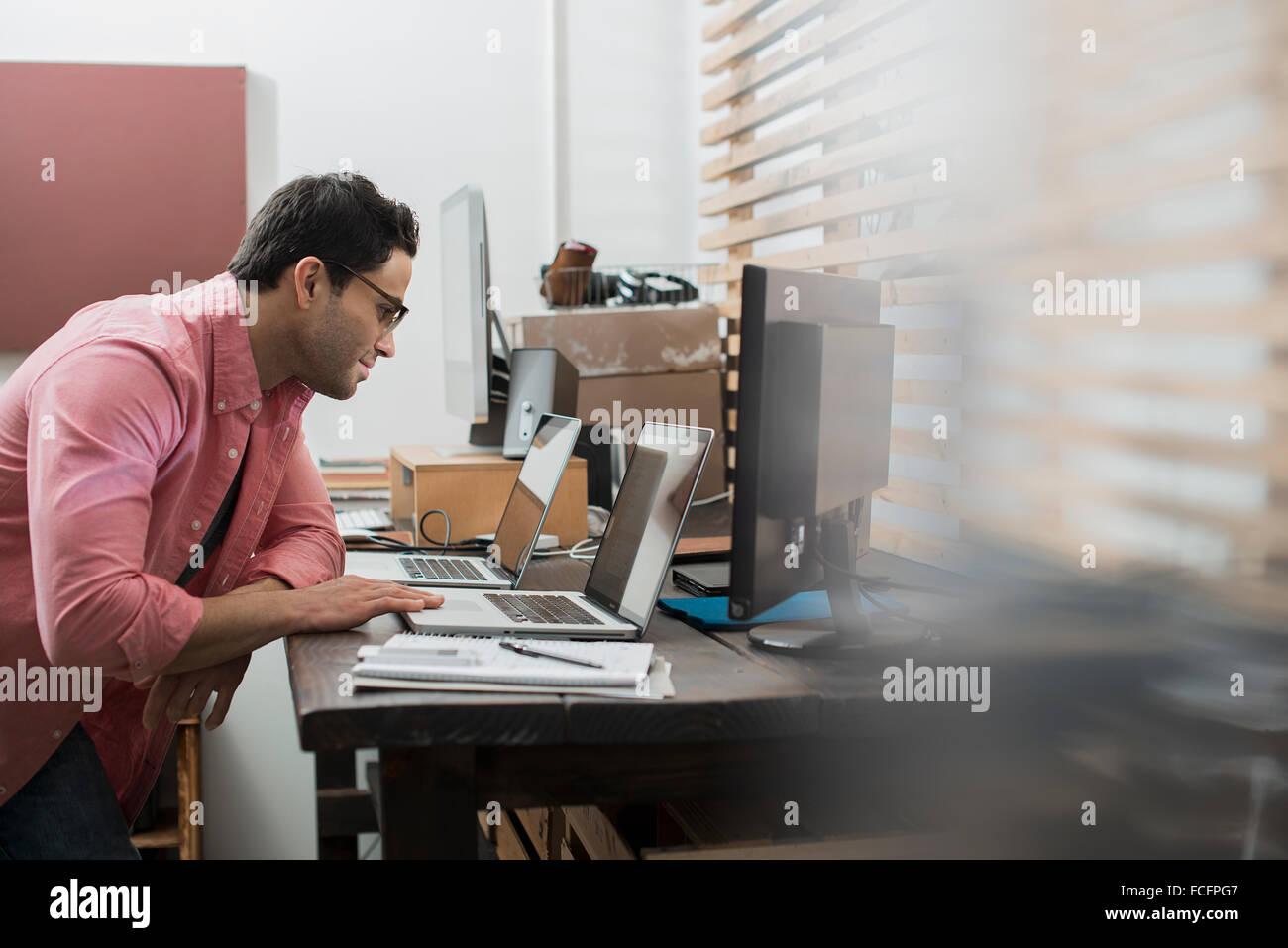 A man in a home office with a desk with two laptops, checking ...