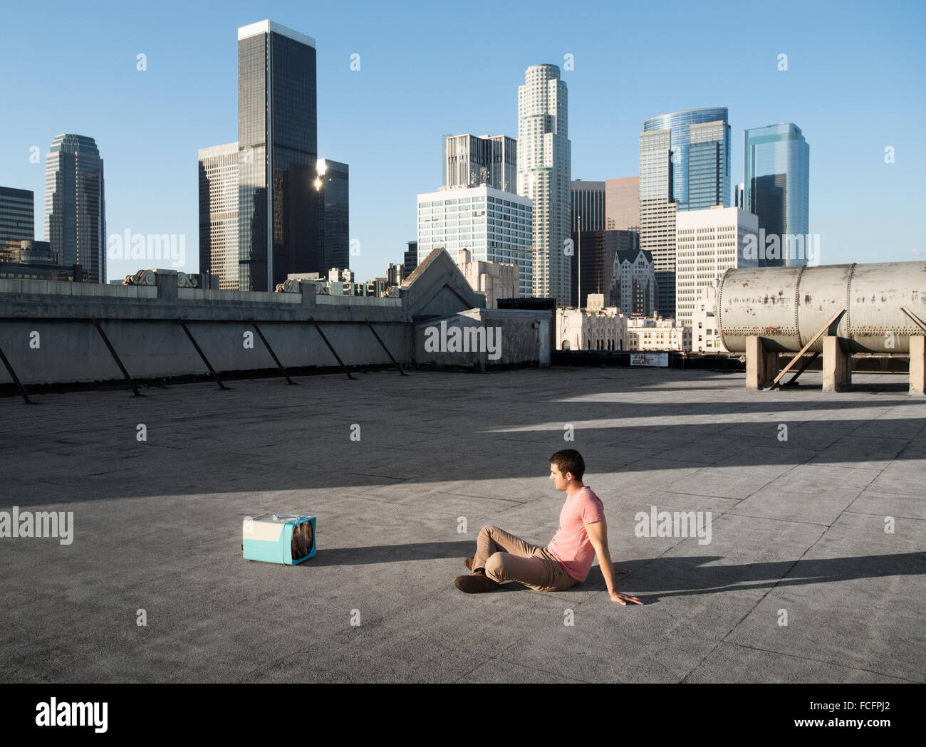A man sitting on a city rooftop watching a small blue portable ...
