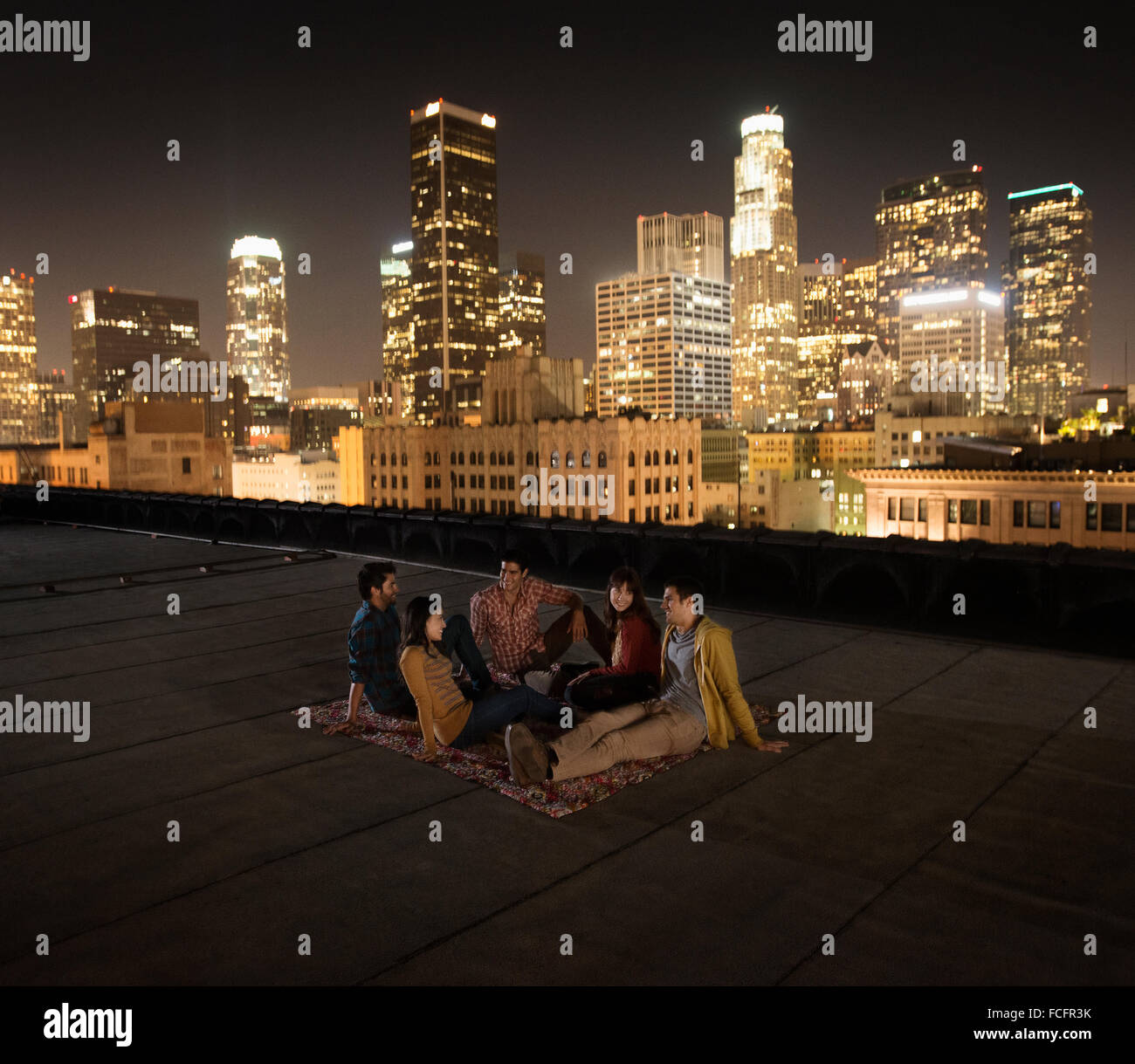 A group of friends gathered on a rooftop overlooking a city lit up at ...