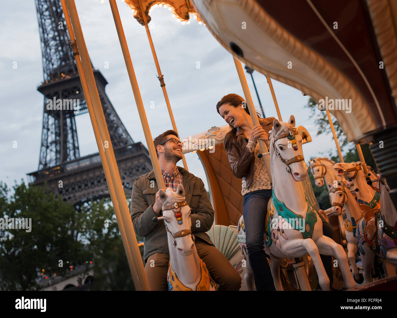A couple, man and woman riding traditional gallopers on a carousel ride ...