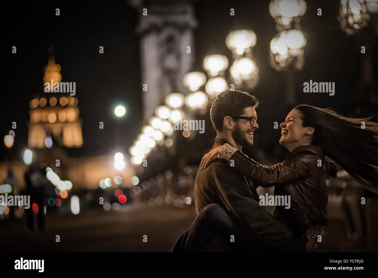 A couple close together facing each other, embracing in a city at night ...