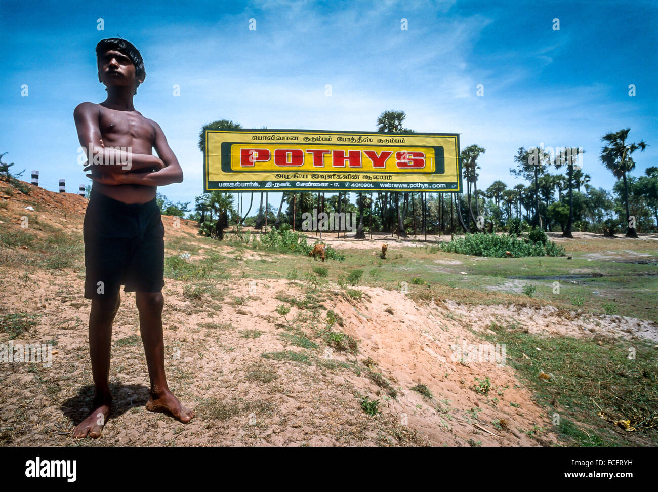 A young boy standing in a field bordered by a huge billboard ...