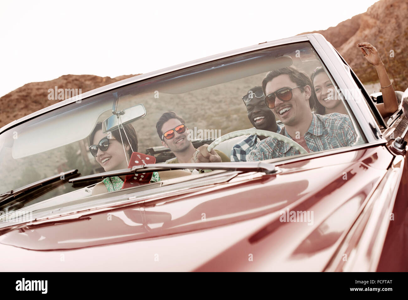 A group of friends in a red open top convertable classic car on a road ...