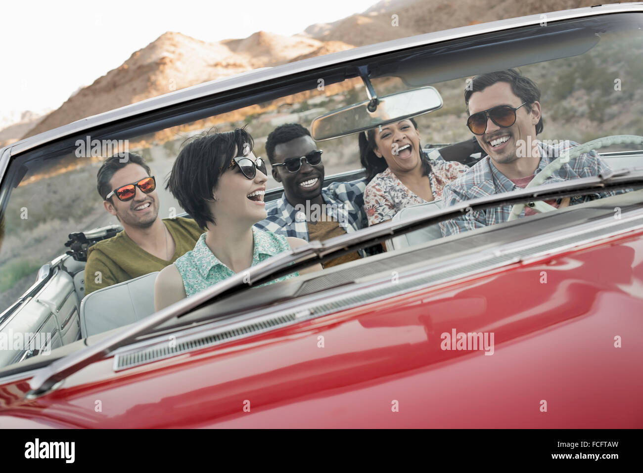 A group of friends in a red open top convertable classic car on a road ...