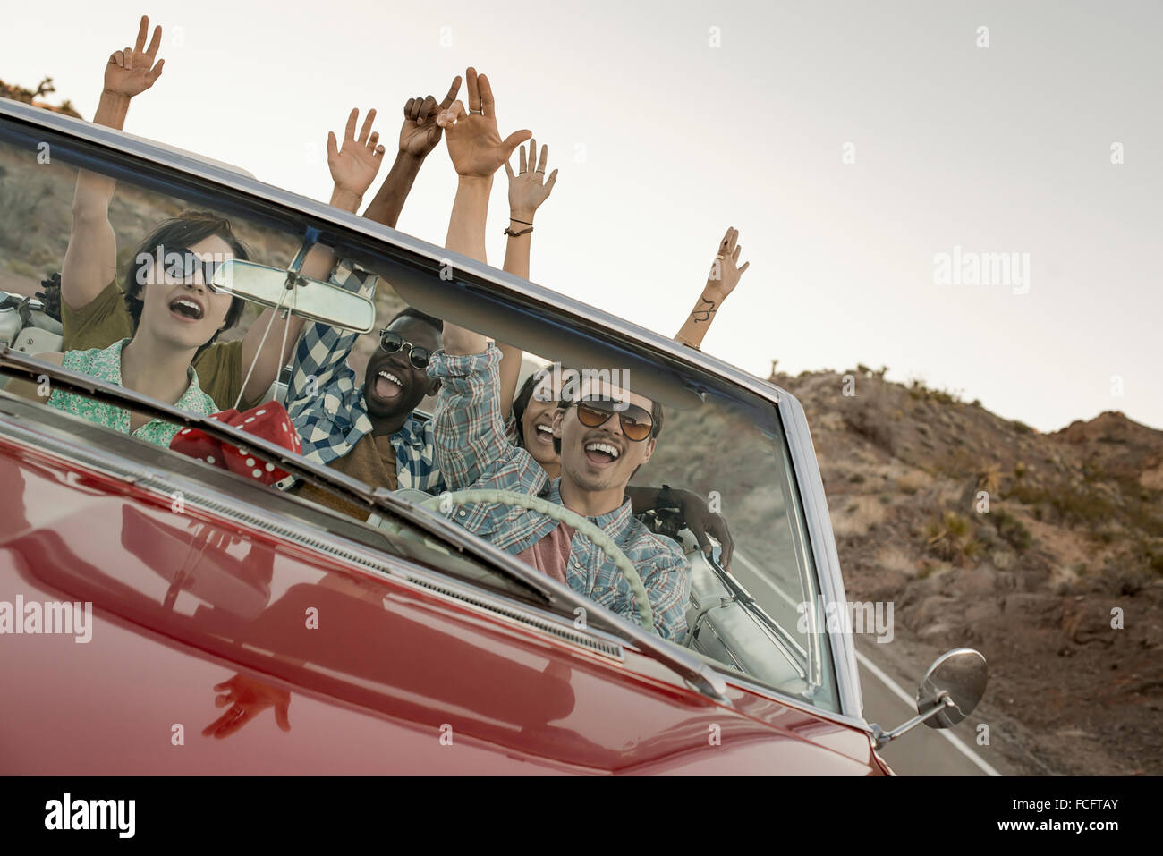 A group of friends in a red open top convertable classic car on a road ...