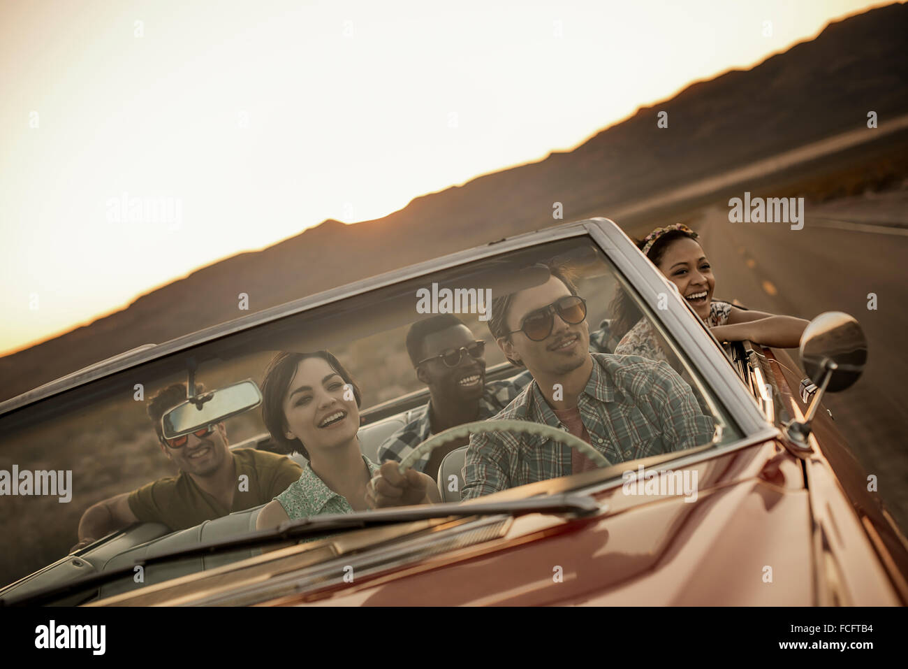 A group of friends in a red open top convertable classic car on a road ...
