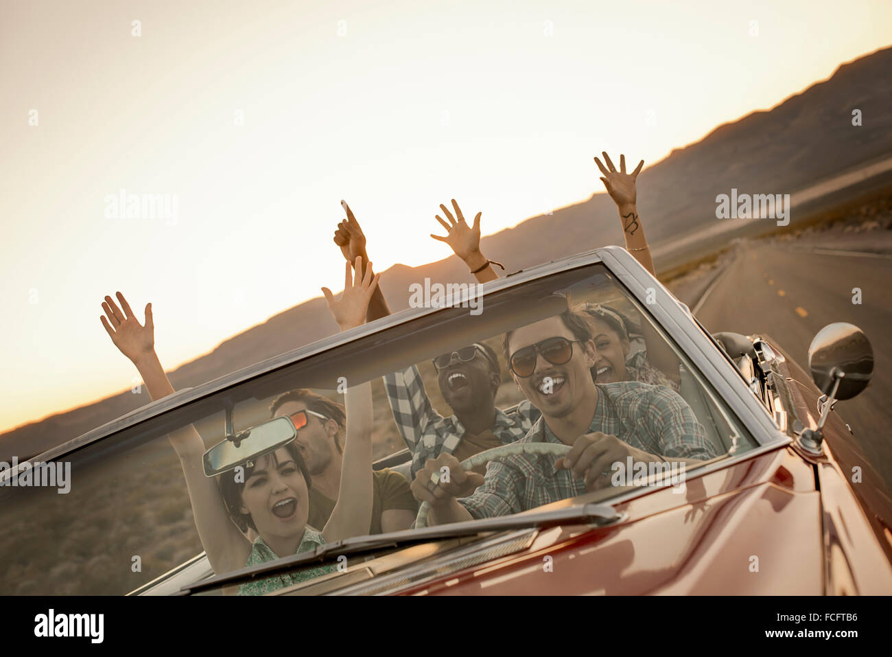 A group of friends in a red open top convertable classic car on a road ...