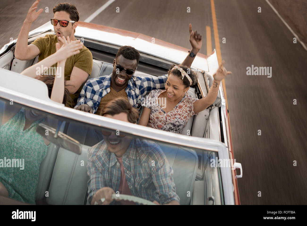 A group of friends in a red open top convertable classic car on a road ...