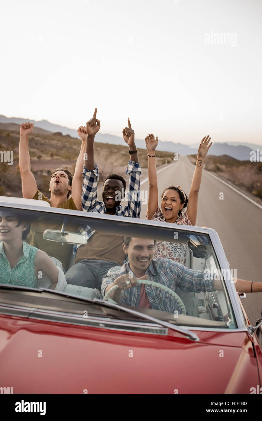 A group of friends in a red open top convertable classic car on a road ...