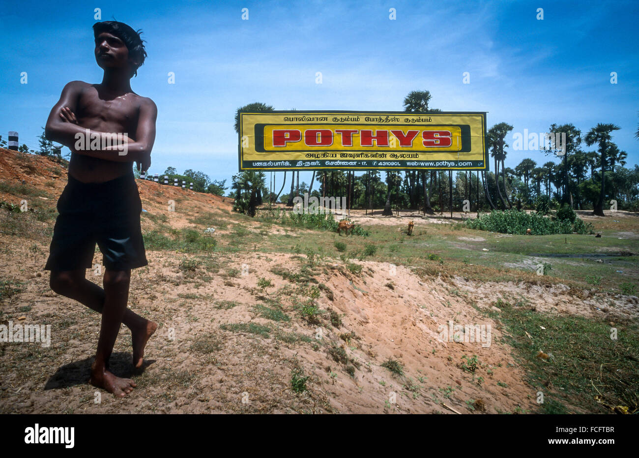 A young boy standing in a field bordered by a huge billboard ...