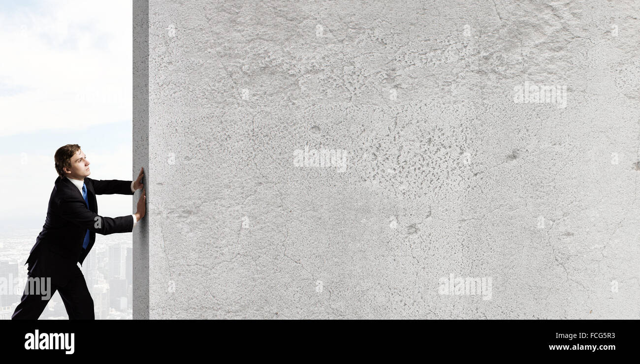 Young businessman making effort to move brick wall Stock Photo - Alamy