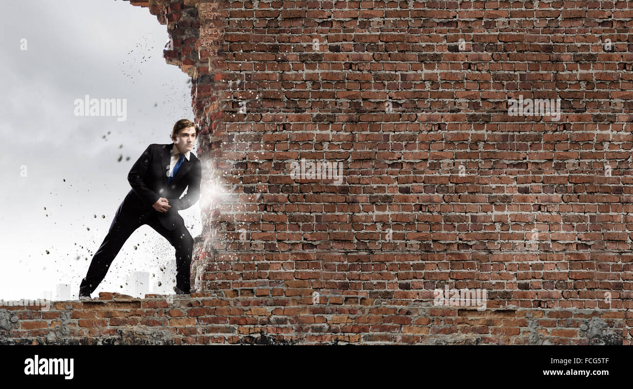 Young businessman making effort to move brick wall Stock Photo - Alamy