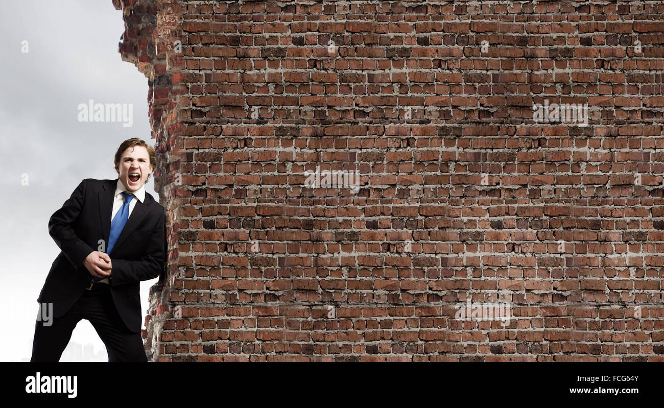Young businessman making effort to move brick wall Stock Photo - Alamy