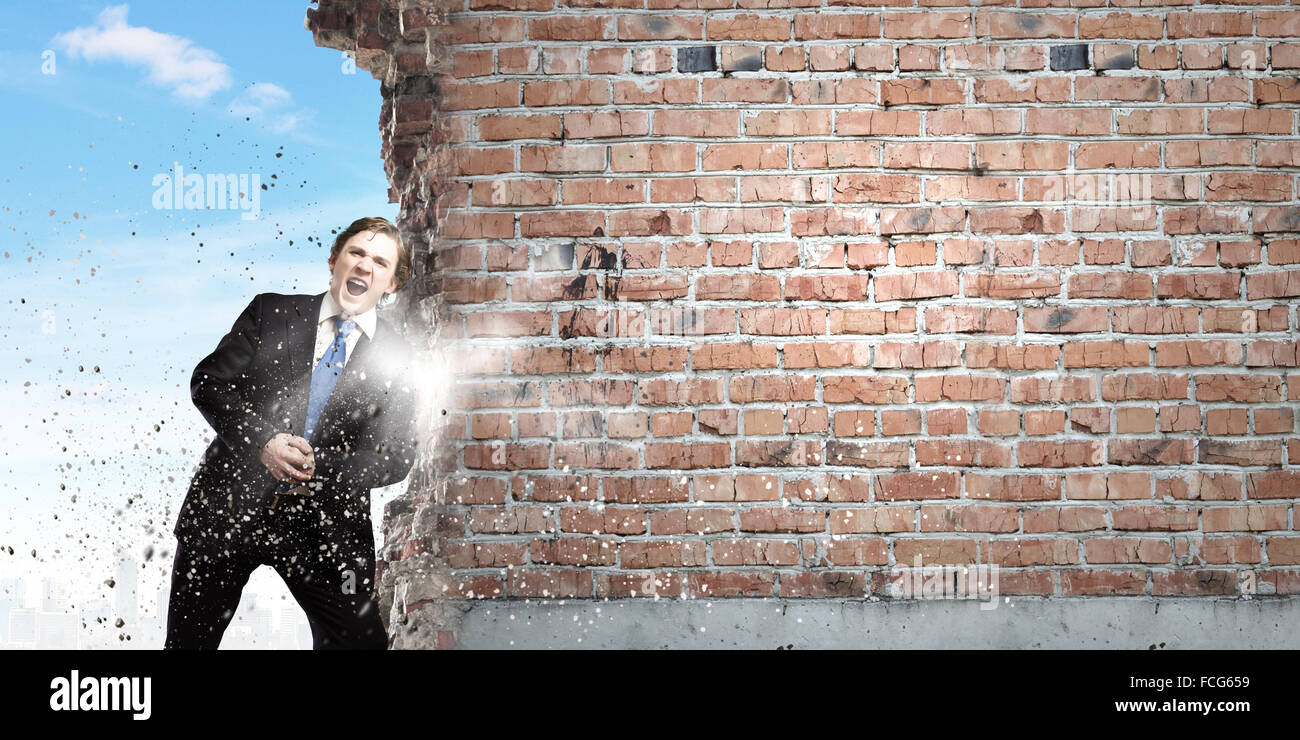 Young businessman making effort to move brick wall Stock Photo - Alamy