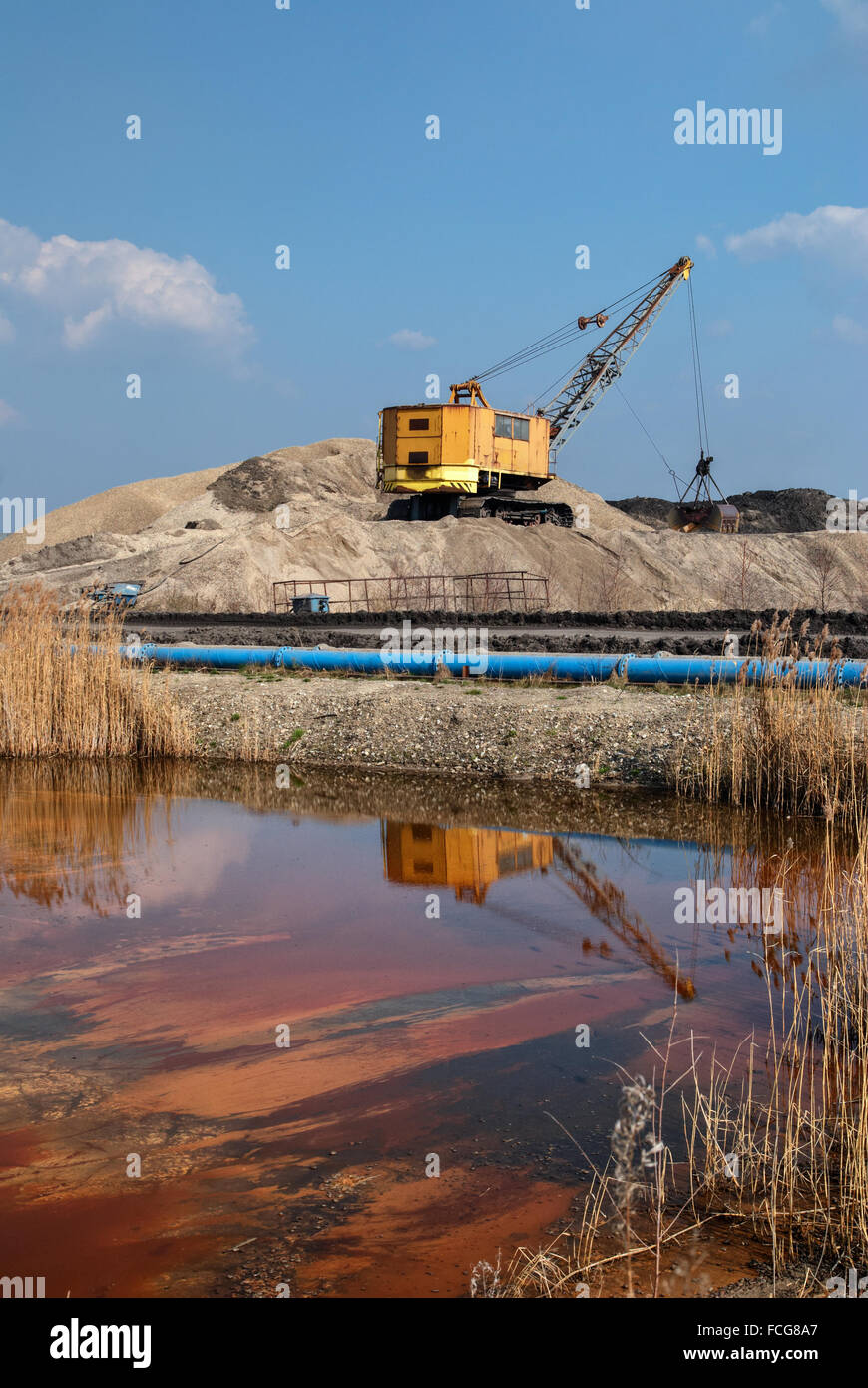 Rope excavator for mining sludge among piles of sand, water tank with ...
